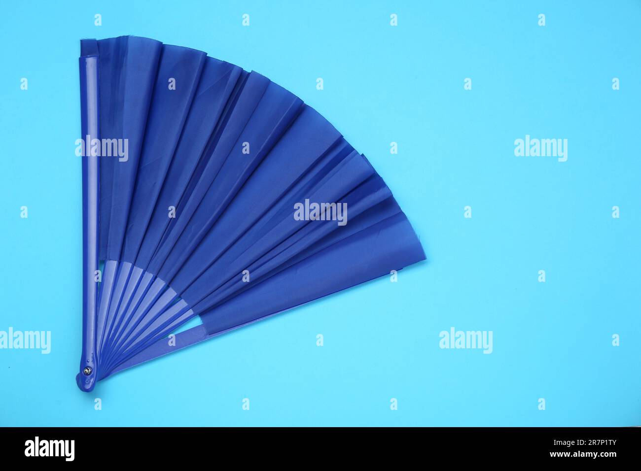 Bright color hand fan on light blue background, top view. Space for ...