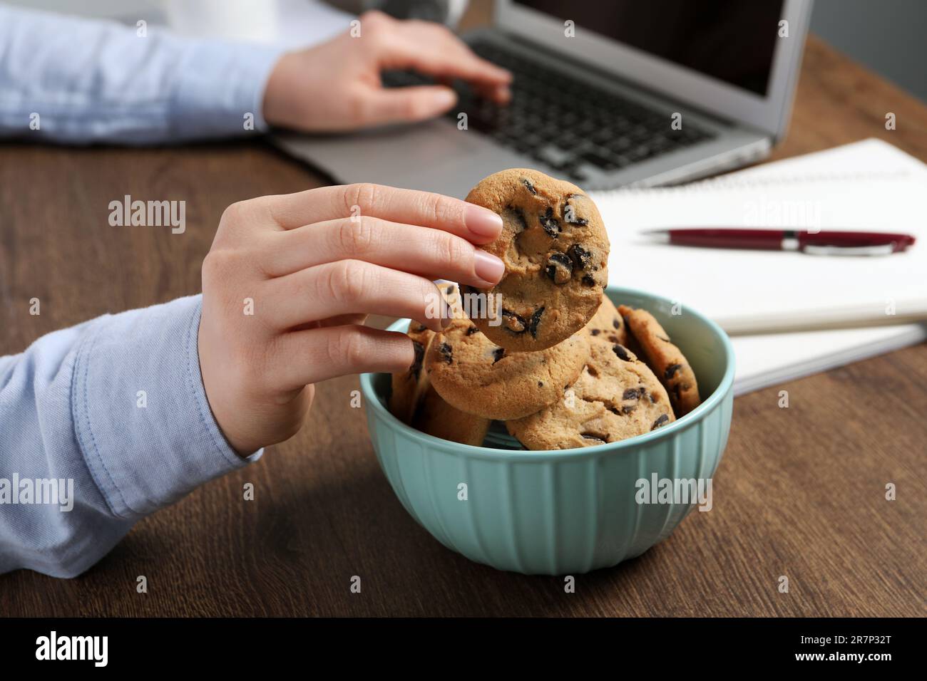 Office worker taking chocolate chip cookie from bowl at workplace ...