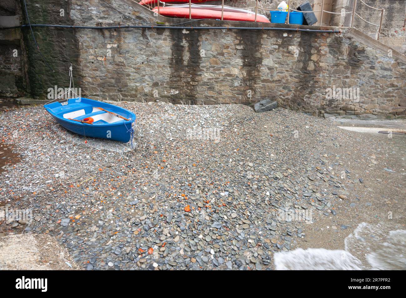 Modern blue plastic dinghy on stony beach by rock wall in Riomaggiore ...