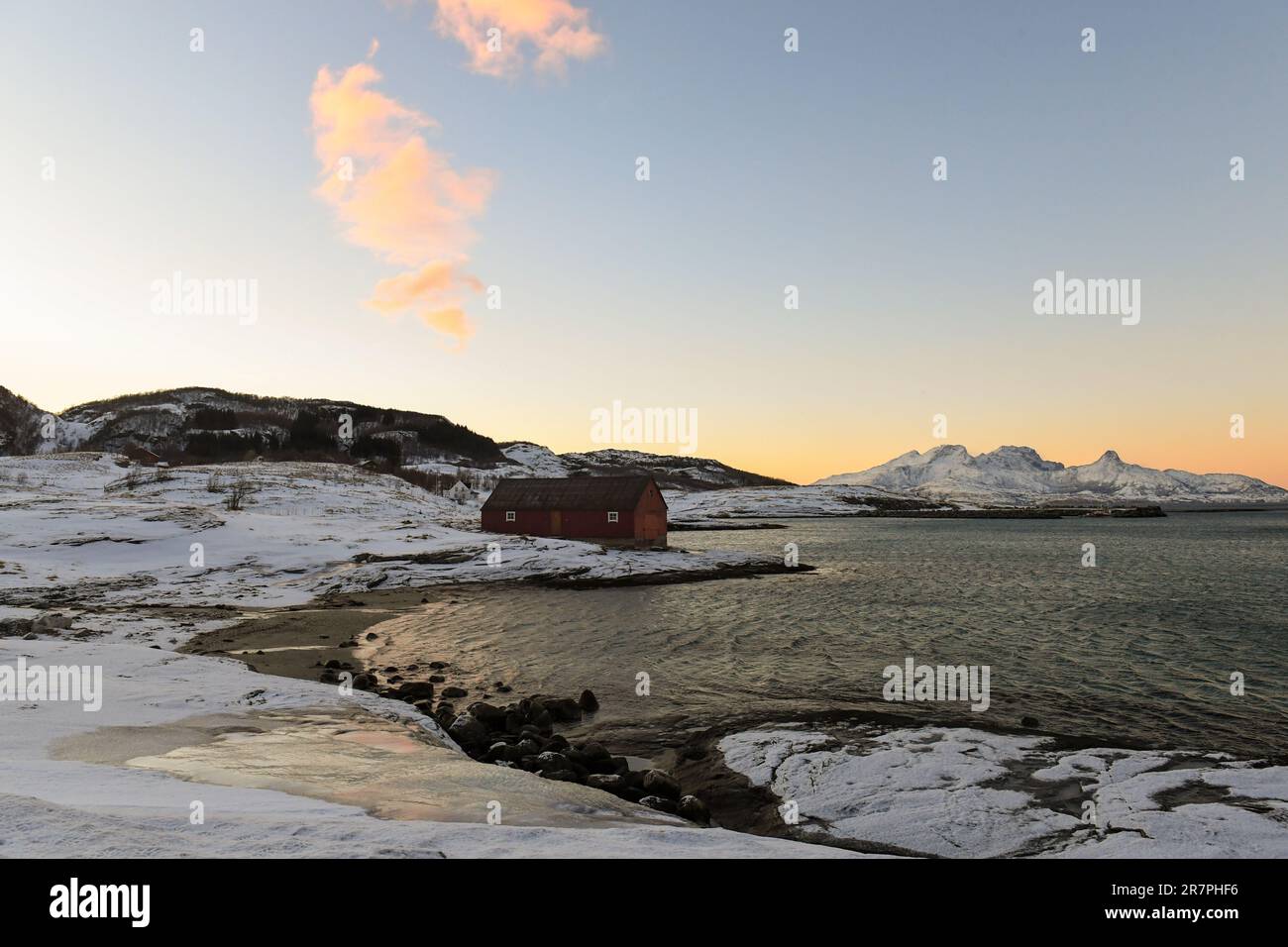 A traditional norwegian red barn enclosed by rugged mountains and snow ...
