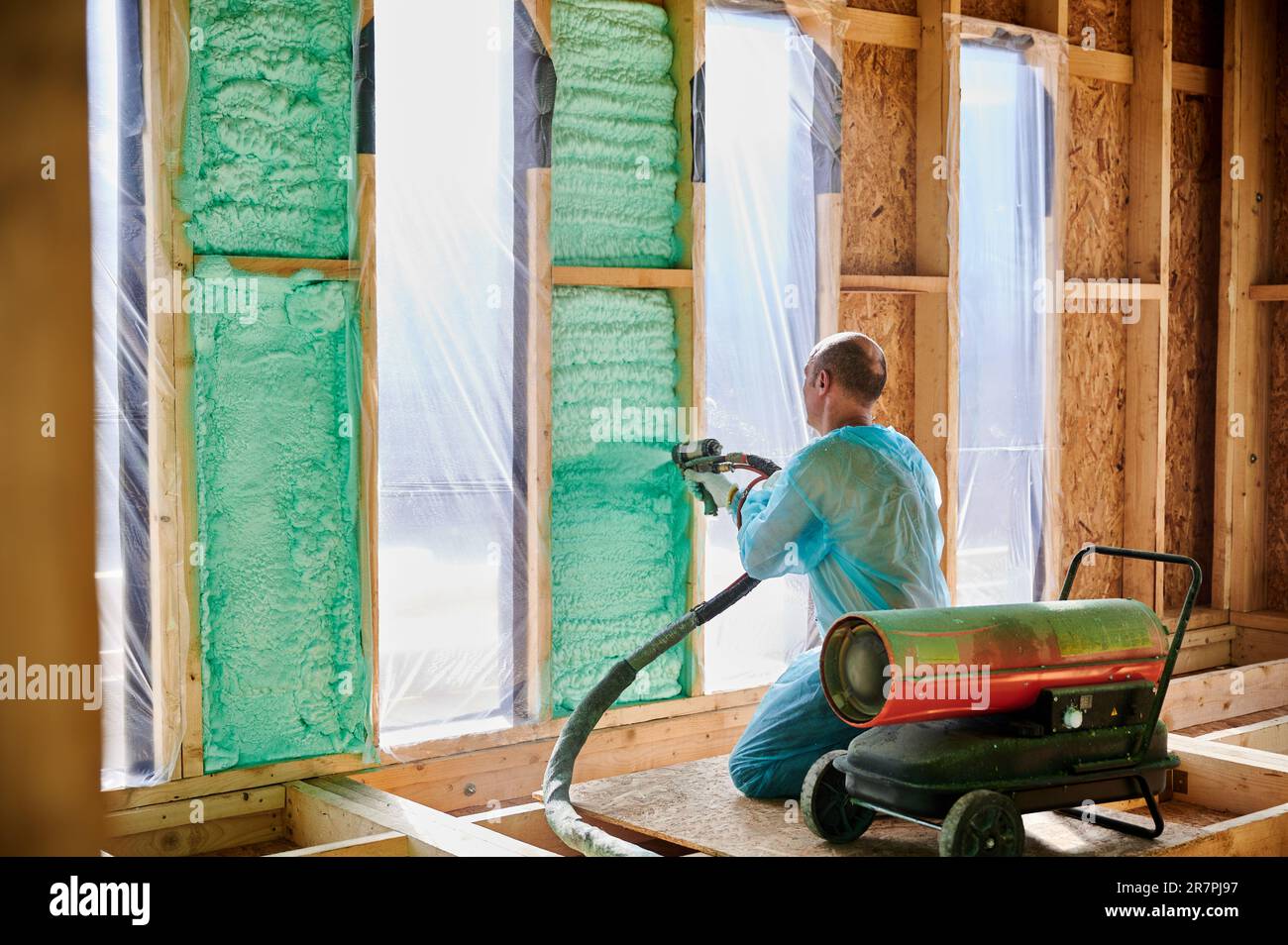 Male builder insulating wooden frame house. Man worker spraying ...