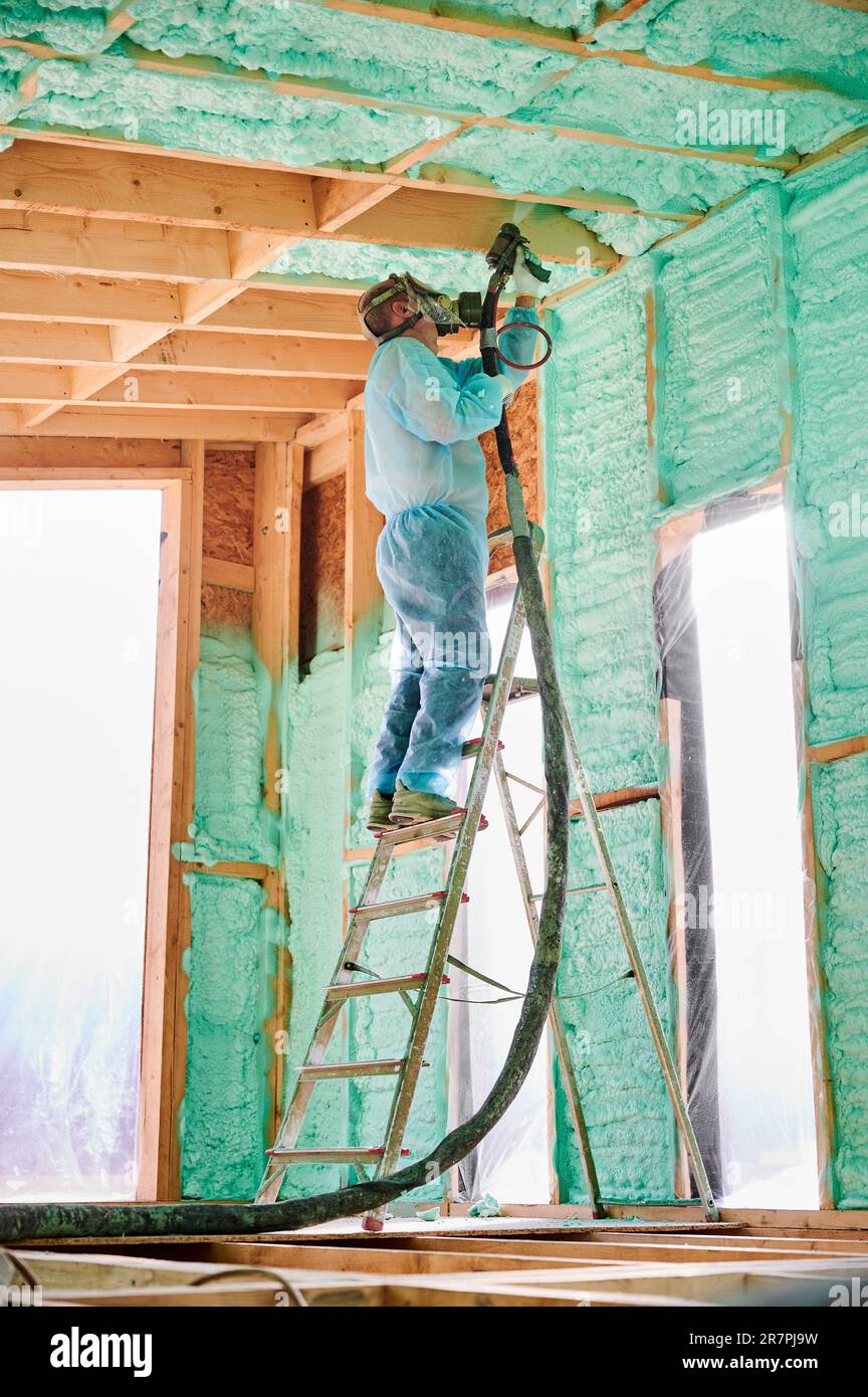 Male builder insulating wooden frame house. Man worker spraying ...