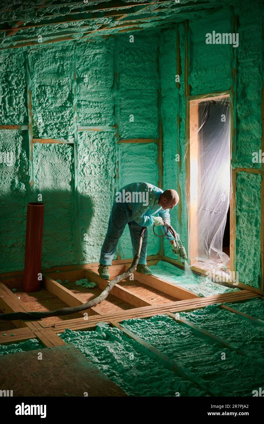 Male builder insulating wooden frame house. Man worker spraying ...