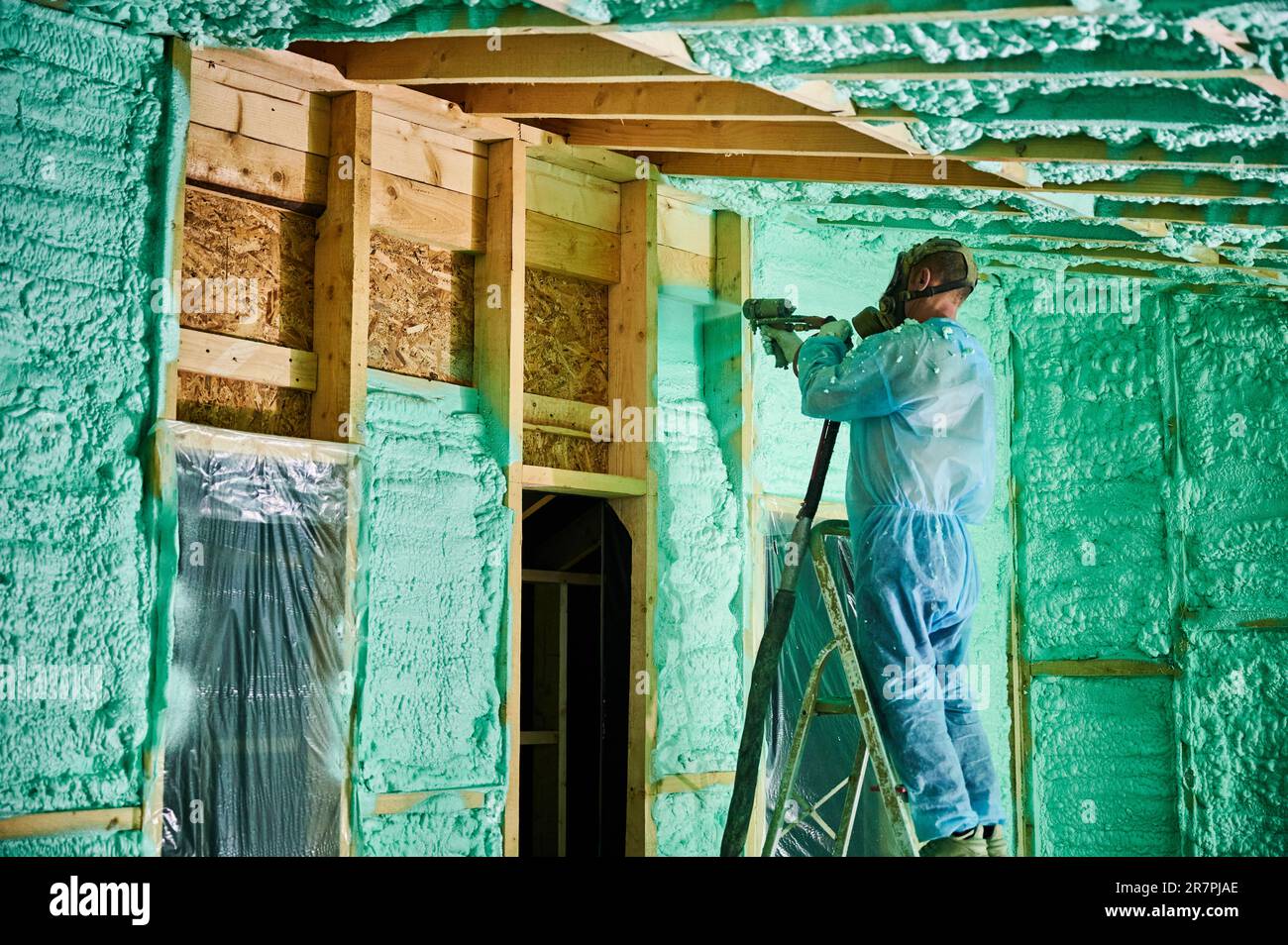 Male builder insulating wooden frame house. Man worker spraying ...