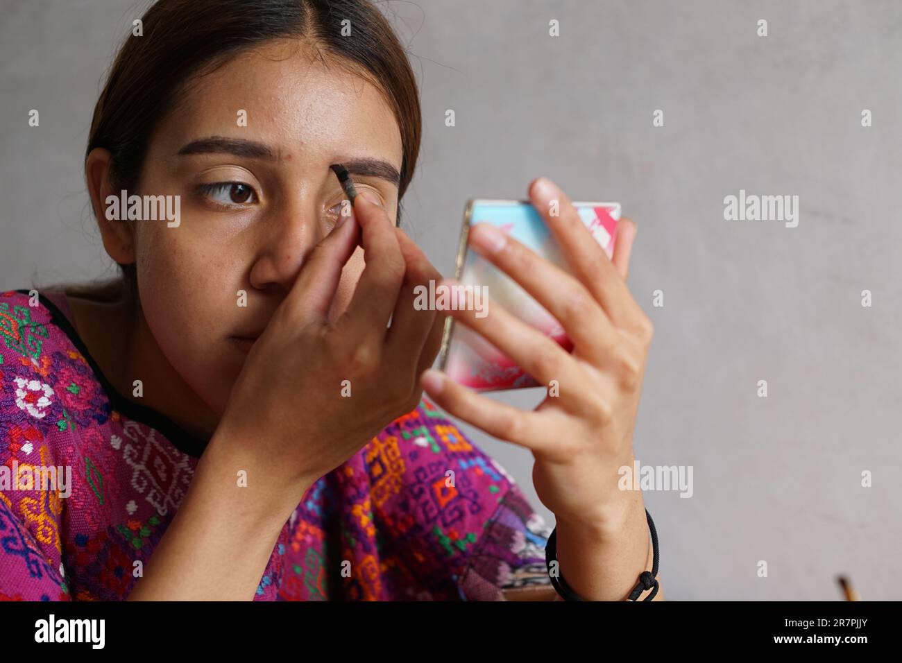 Guatemalan mayan girl putting on makeup in traditional huipil dress ...