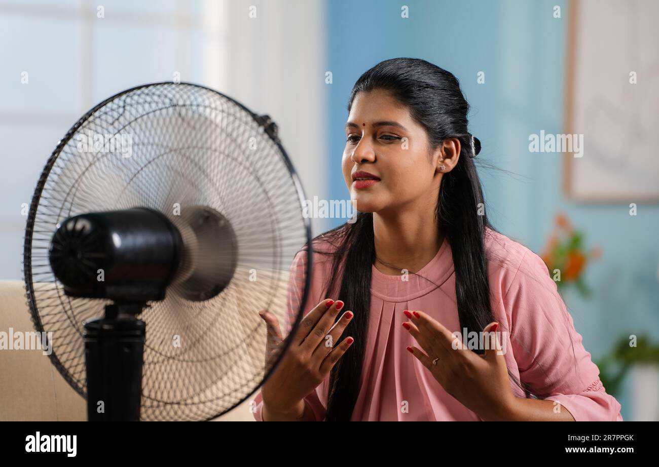 Indian woman using electric fan during hot summer day by sitting in ...