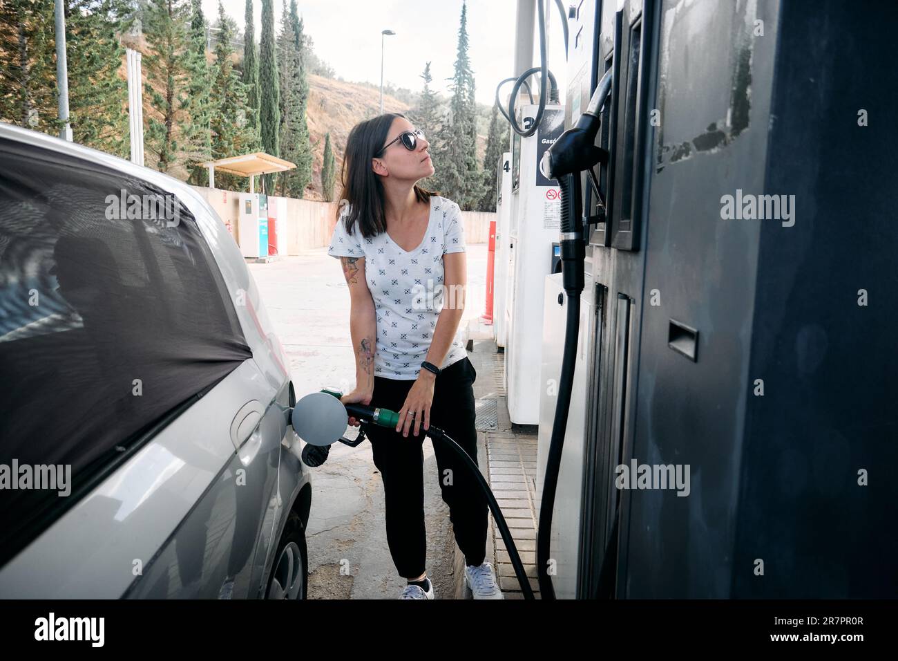 a young brunette woman refueling herself at a small gas station at ...