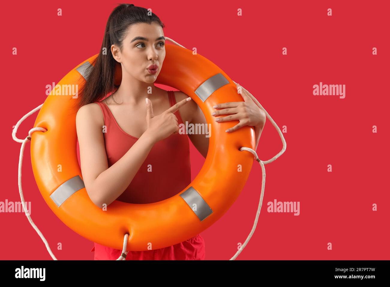 Female lifeguard with ring buoy pointing at something on red background ...