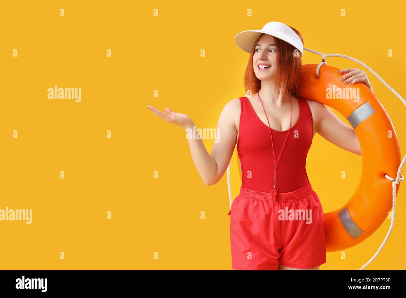 Female lifeguard with ring buoy showing something on yellow background ...