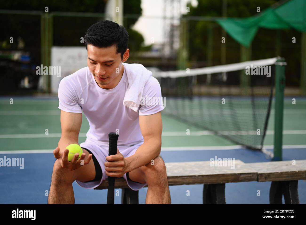 Tired sportsman holding ball racket sitting on the bench at tennis ...