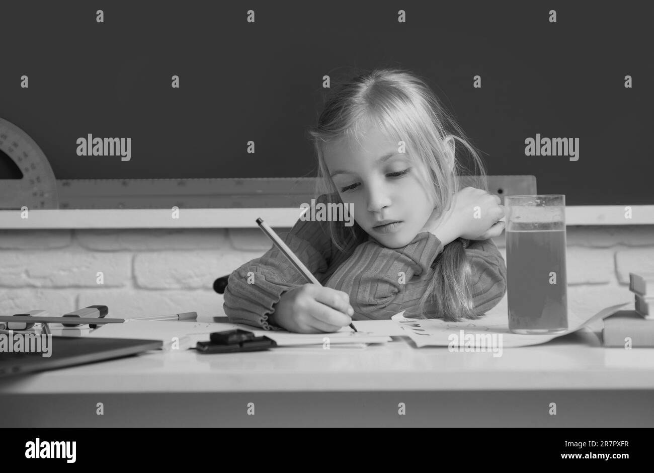 Portrait of cute little schoolgirl writing in book with classmates in ...
