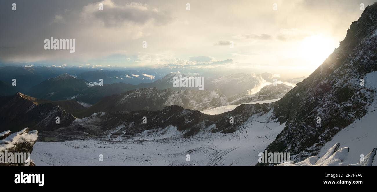 Sun setting behind mountain in high alpine environment with snow and ...