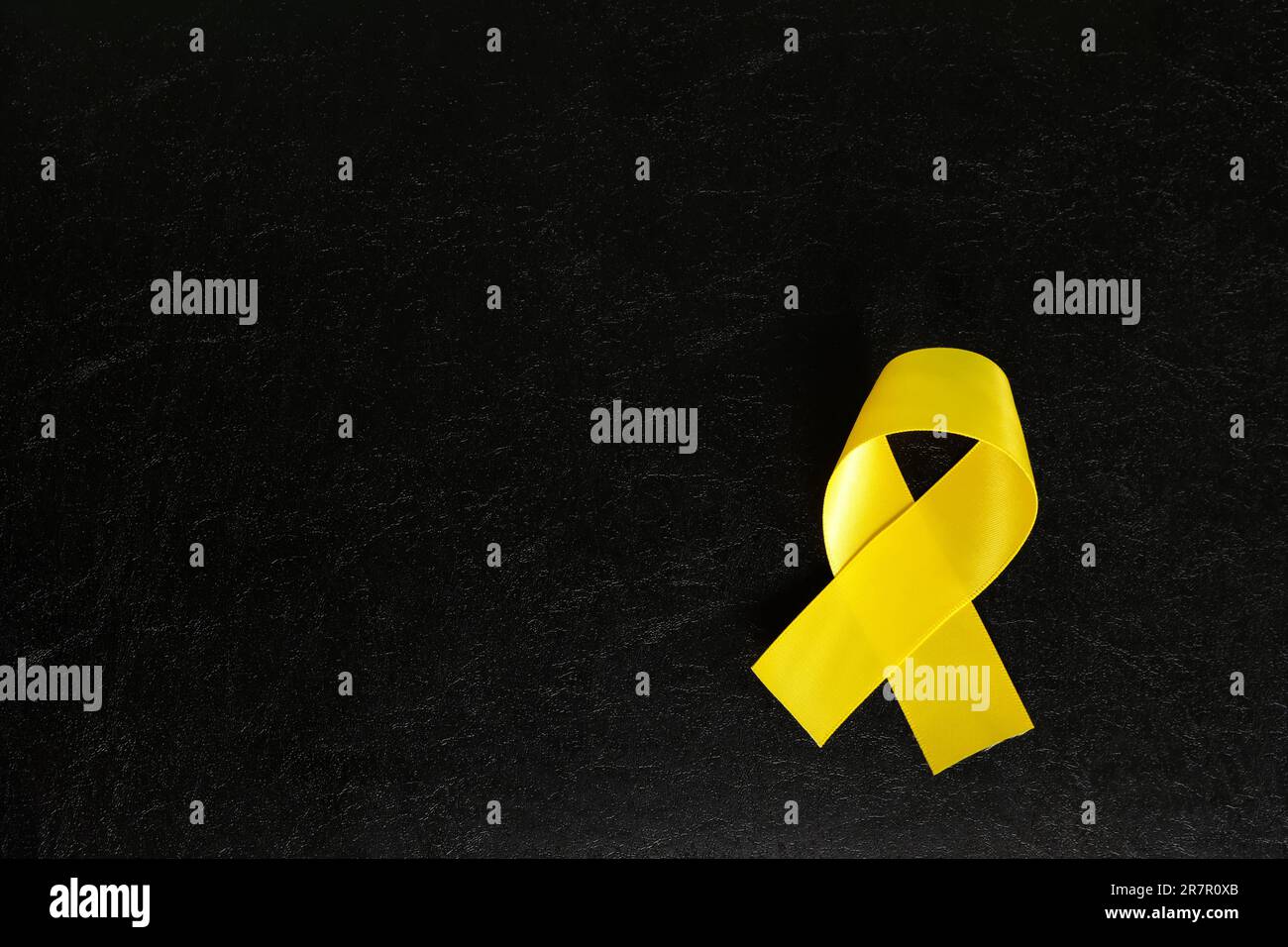 Yellow cancer awareness ribbon isolated on dark black background. Bone ...