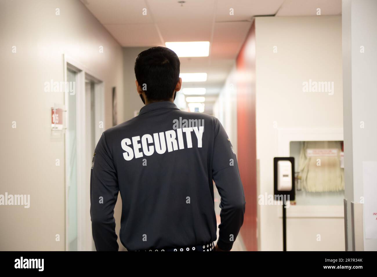 A man wearing security clothes in a hallway with his back to the camera ...