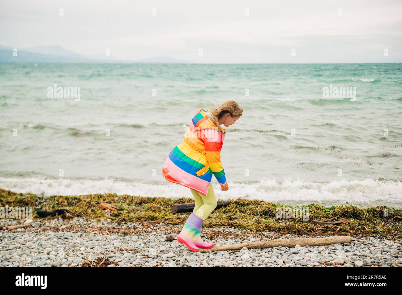 Cute little girl playing by the lake on a windy day, wearing colorful ...
