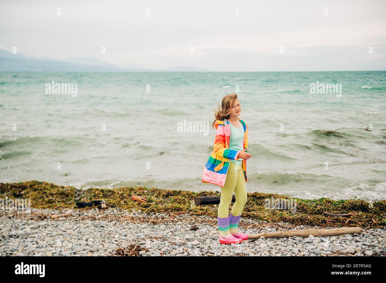 Cute little girl playing by the lake on a windy day, wearing colorful ...