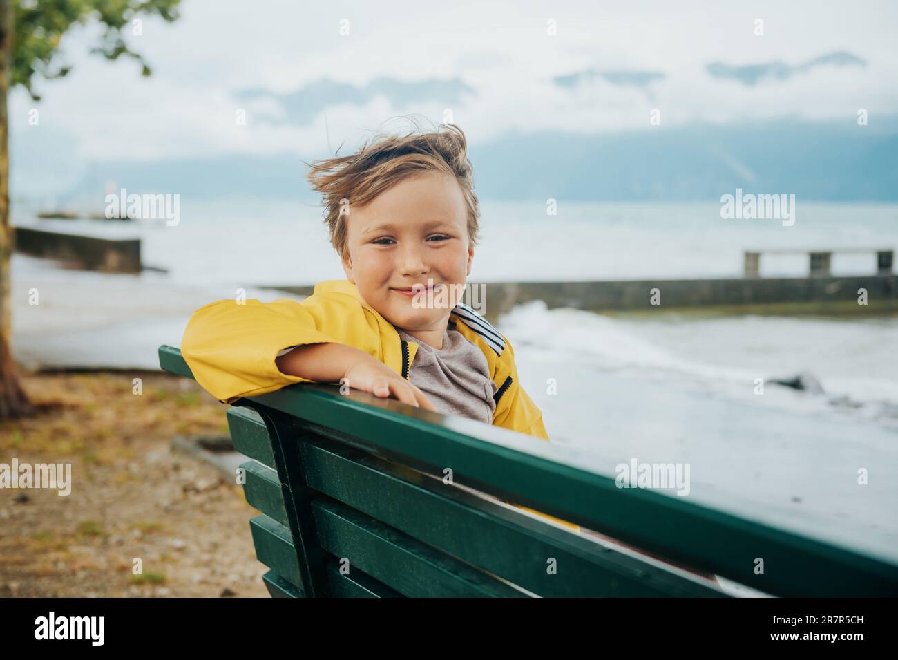 Cute little boy resting on a bench by the lake on a very windy day ...