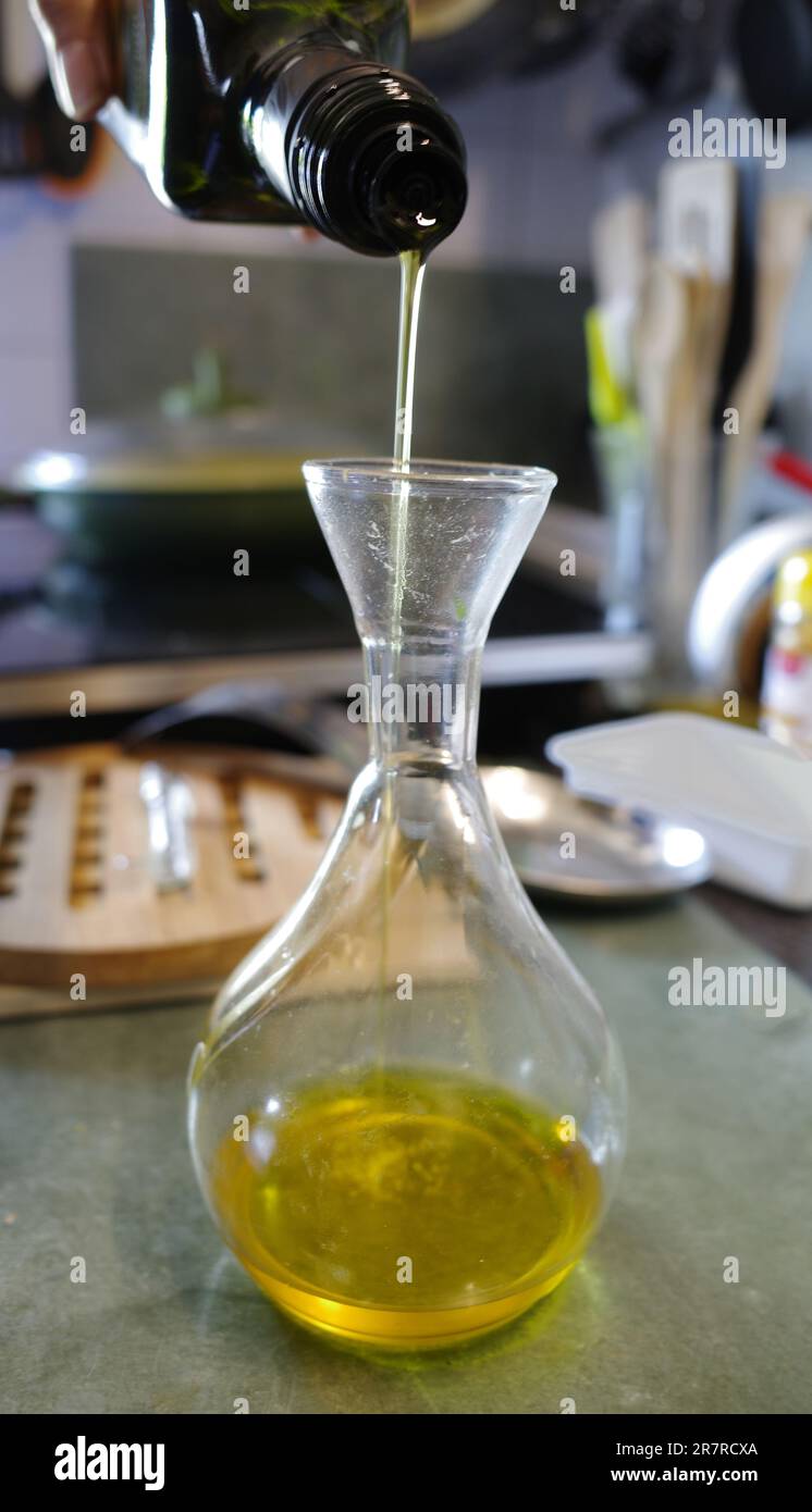 Pouring olive oil into an oil dispenser. Kitchen utensils in the ...