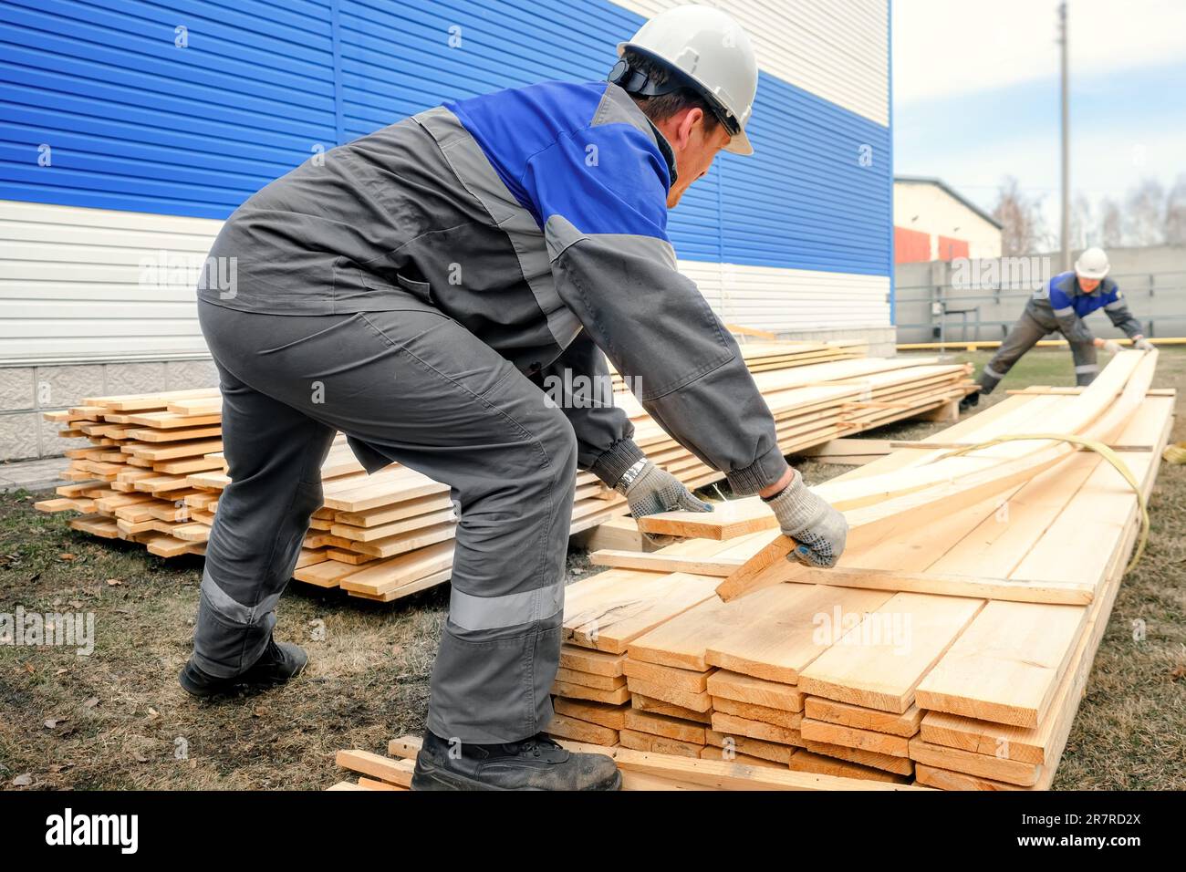 Workers in hard hats unload and rearrange wooden boards on a summer day ...