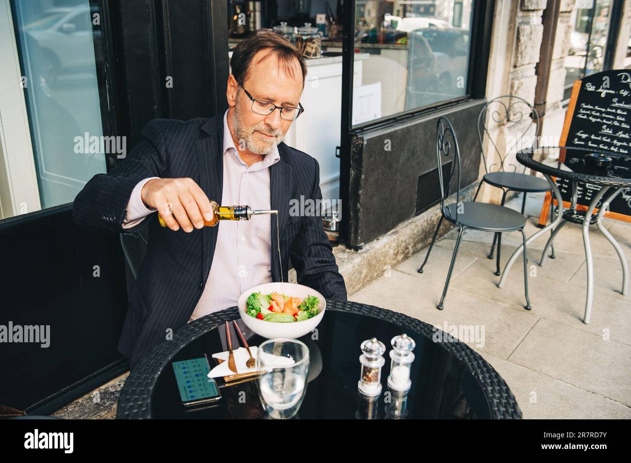 Businessman having lunch on a terrace in outdoor cafe, wearing a suit ...
