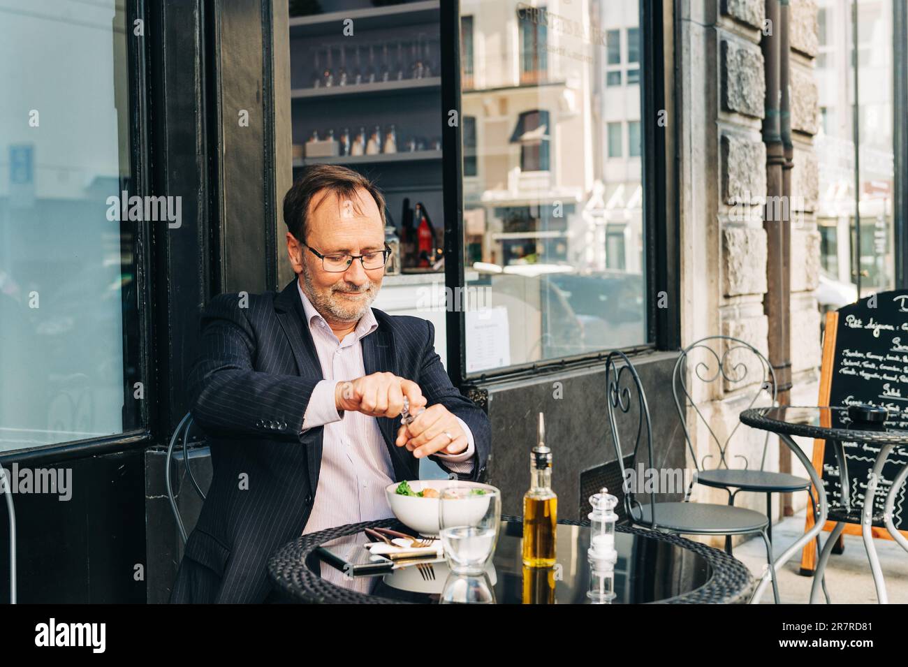 Businessman having lunch on a terrace in outdoor cafe, wearing a suit ...