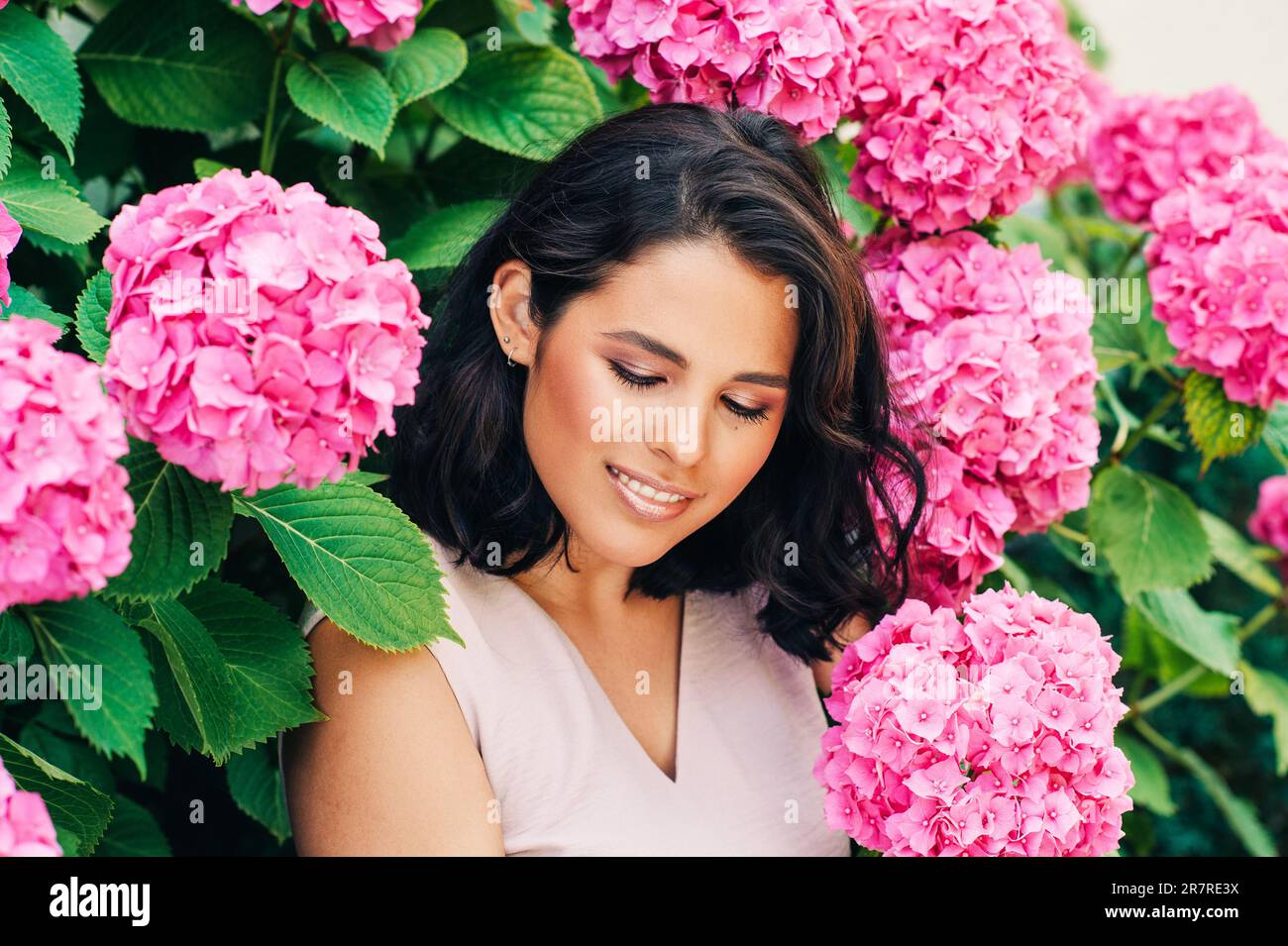 Outdoor portrait of beautiful young woman posing in pink hydrangea ...