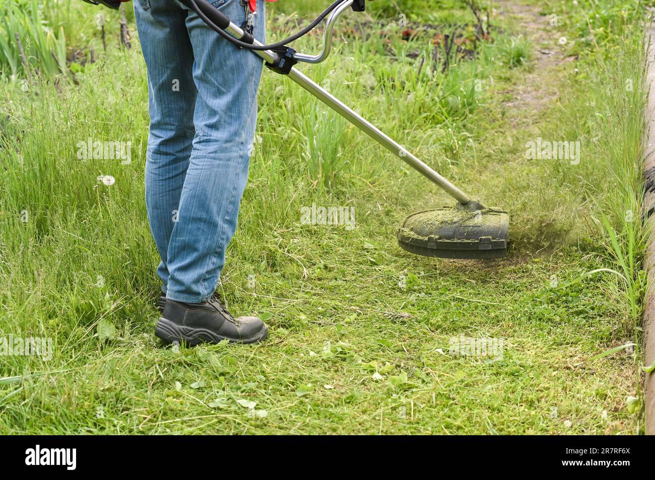 Worker mowing tall grass with electric or petrol lawn trimmer in city ...