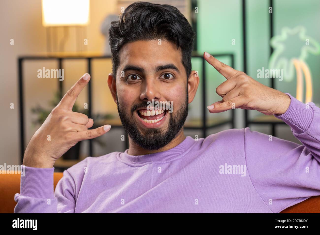Overjoyed delighted young indian man showing rock n roll gesture by ...