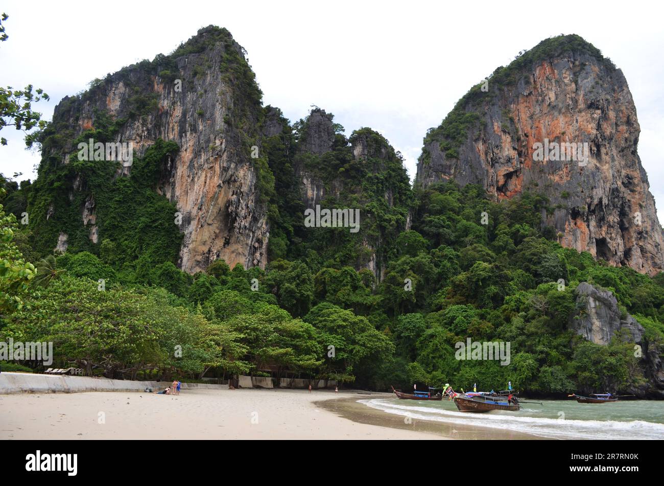 Two mountains next to sandy beach with long tail boat in ocean on ...