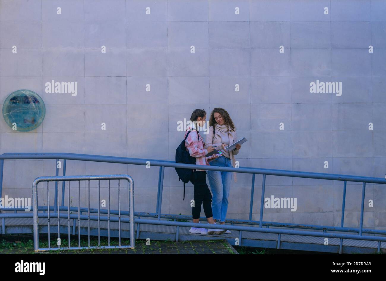 Girls discussing school subject while leaning on metal railing. Front ...