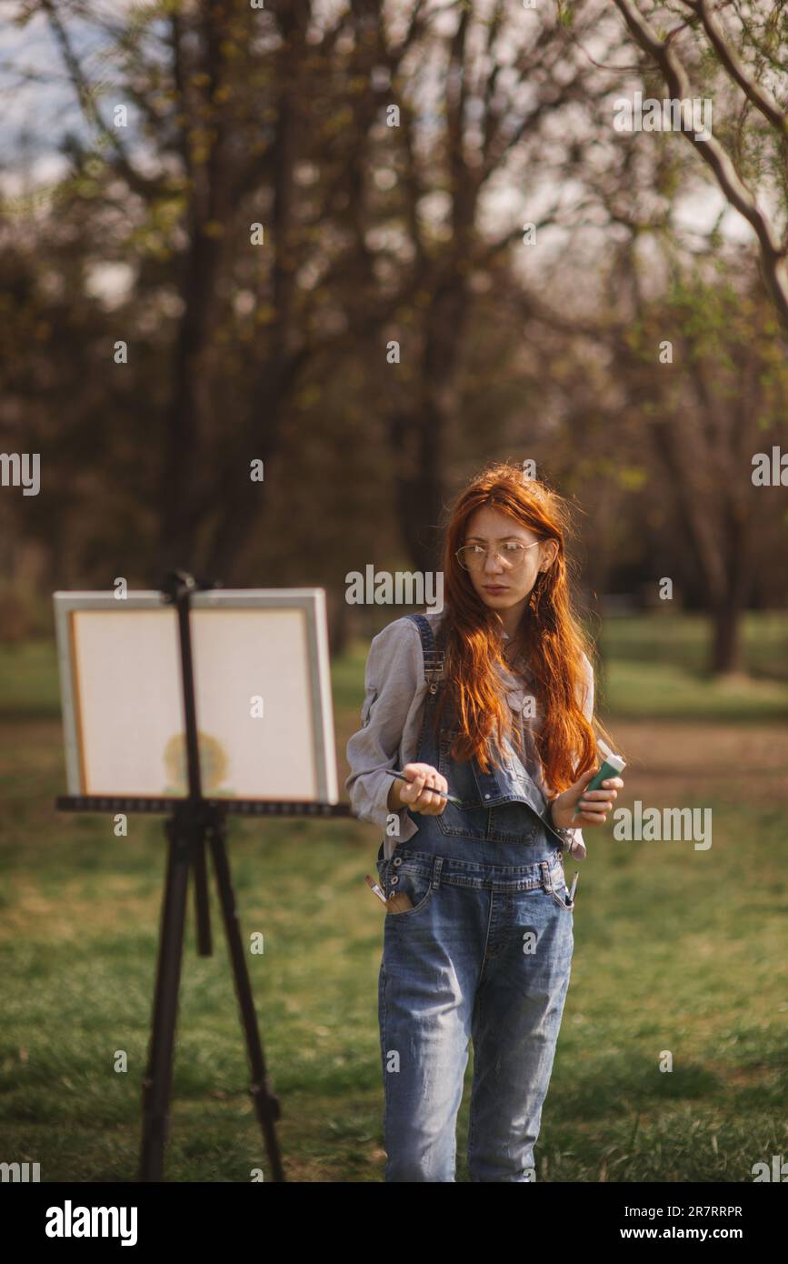Beautiful female artist with red hair standing in front of a easel and ...