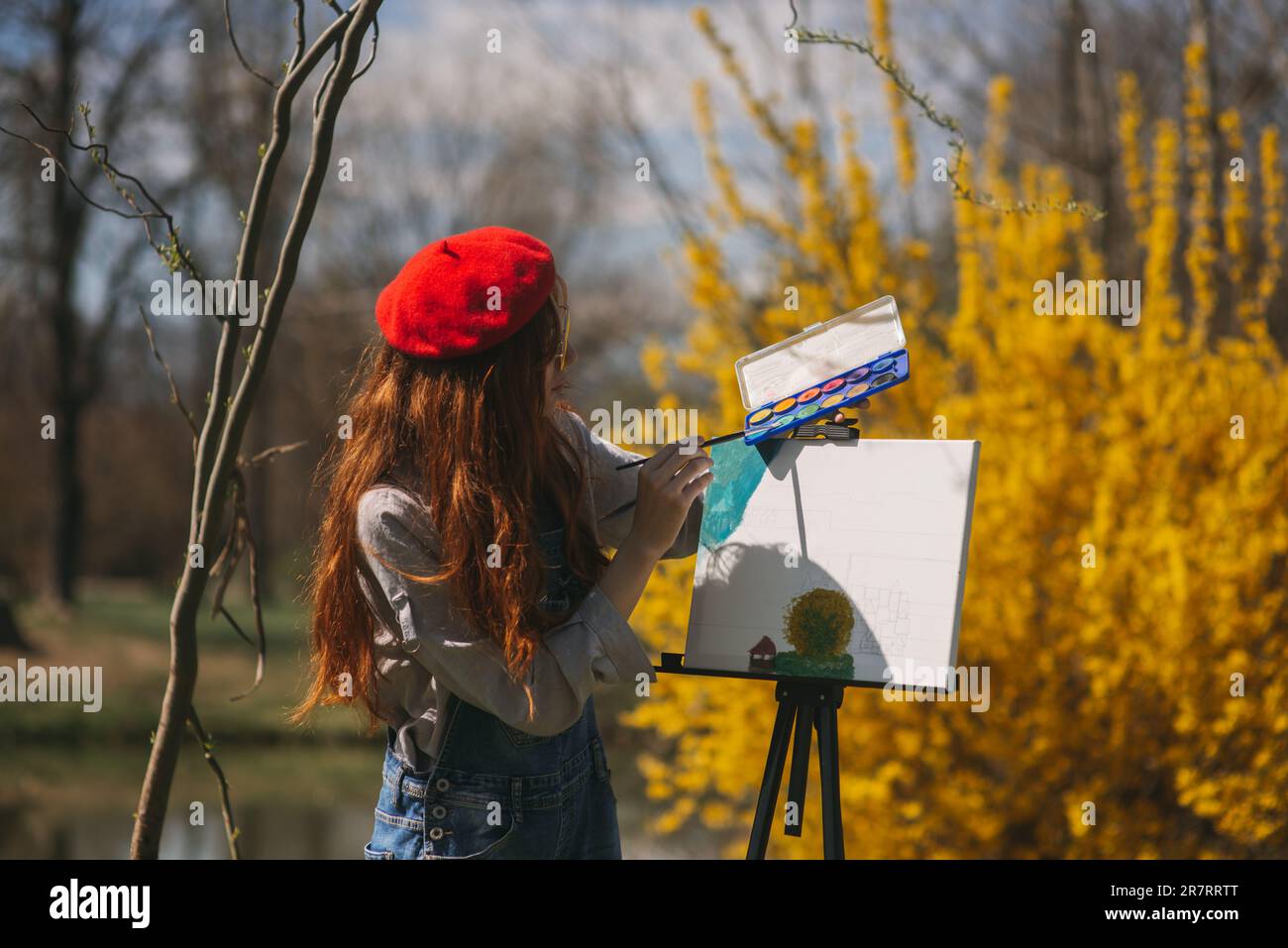 Ginger girl with red hat painting on an easel with her color palette ...