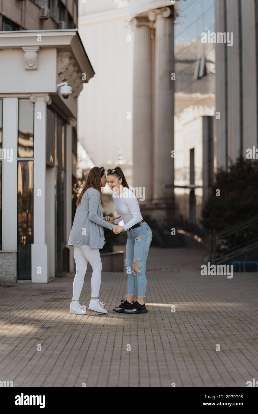 Two young women standing on a sidewalk talking to each other Stock ...