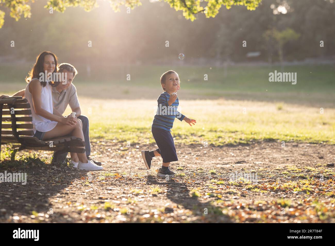 Cute white family in the park - a little boy chasing soap bubbles and ...