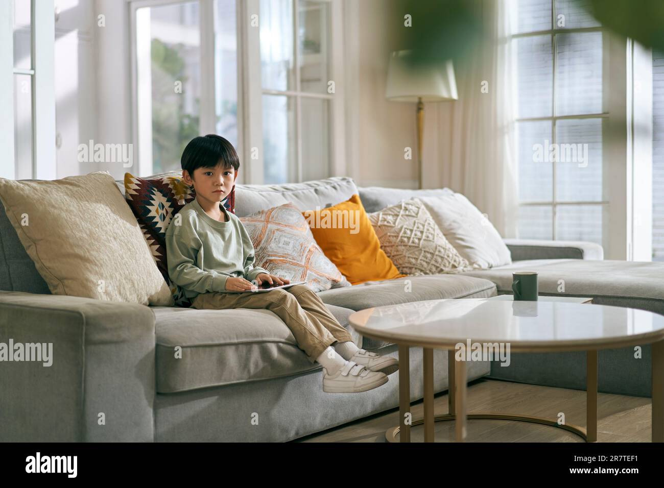 little asian boy sitting on family couch in living room at home looking ...