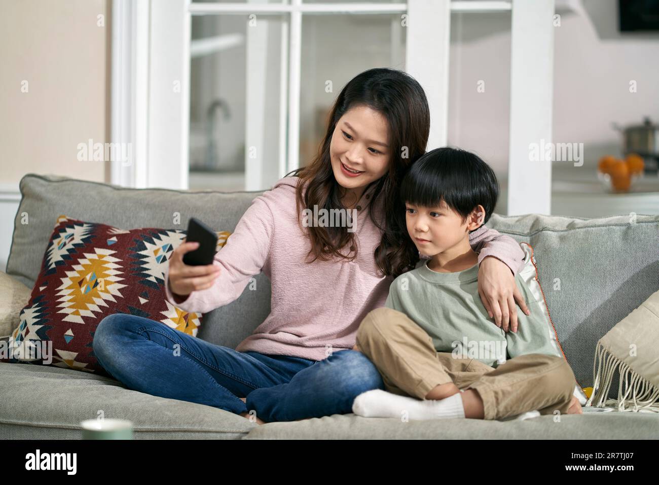 happy asian mother and son sitting on family couch at home taking a ...