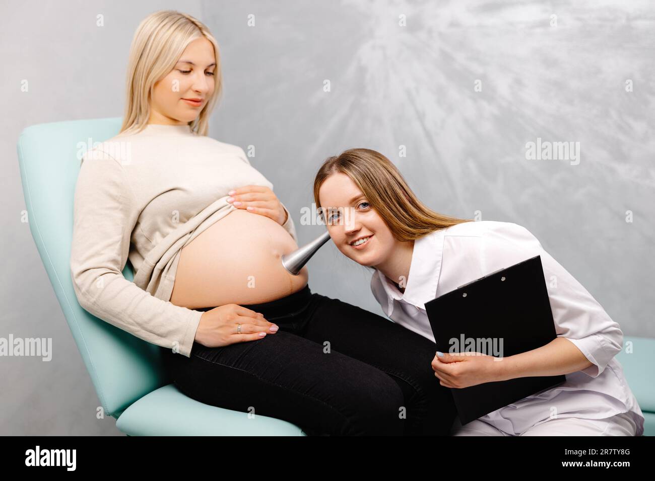 A gynecologist leans a stethoscope to a pregnant woman's belly and ...