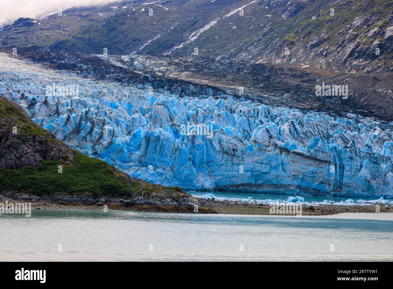 A scenic view of a rugged cliff face and still lake, with a large chunk ...
