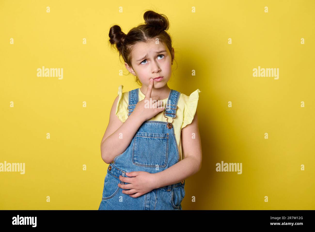 Pensive little kid girl thoughtfully looking aside, putting finger on ...