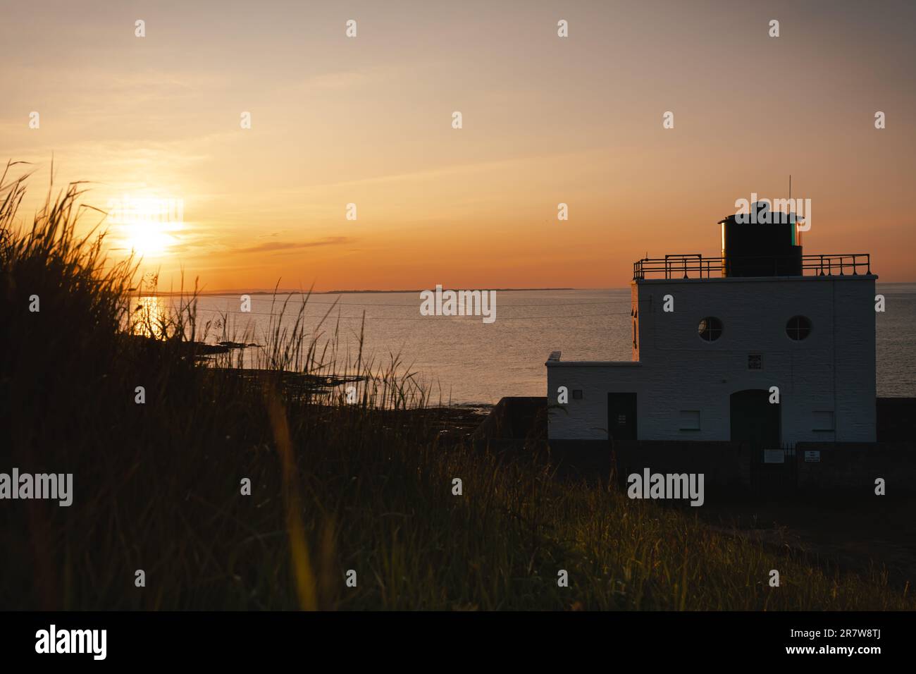 The Bamburgh Lighthouse with its smiley face at sunset with Lindisfarne ...