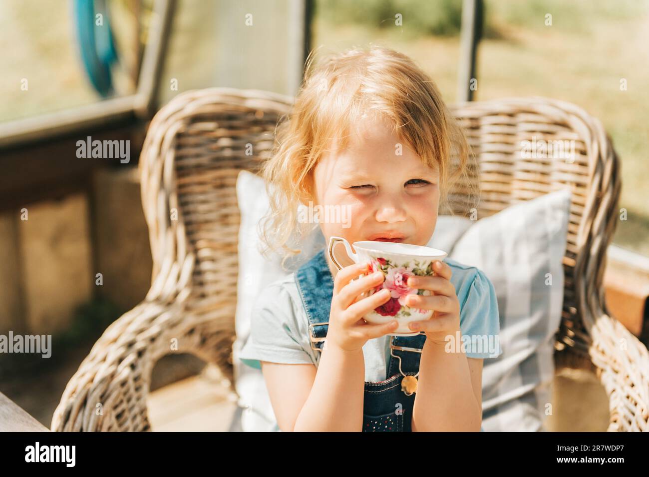 Funny little girl drinking tea on sunny terrace Stock Photo - Alamy