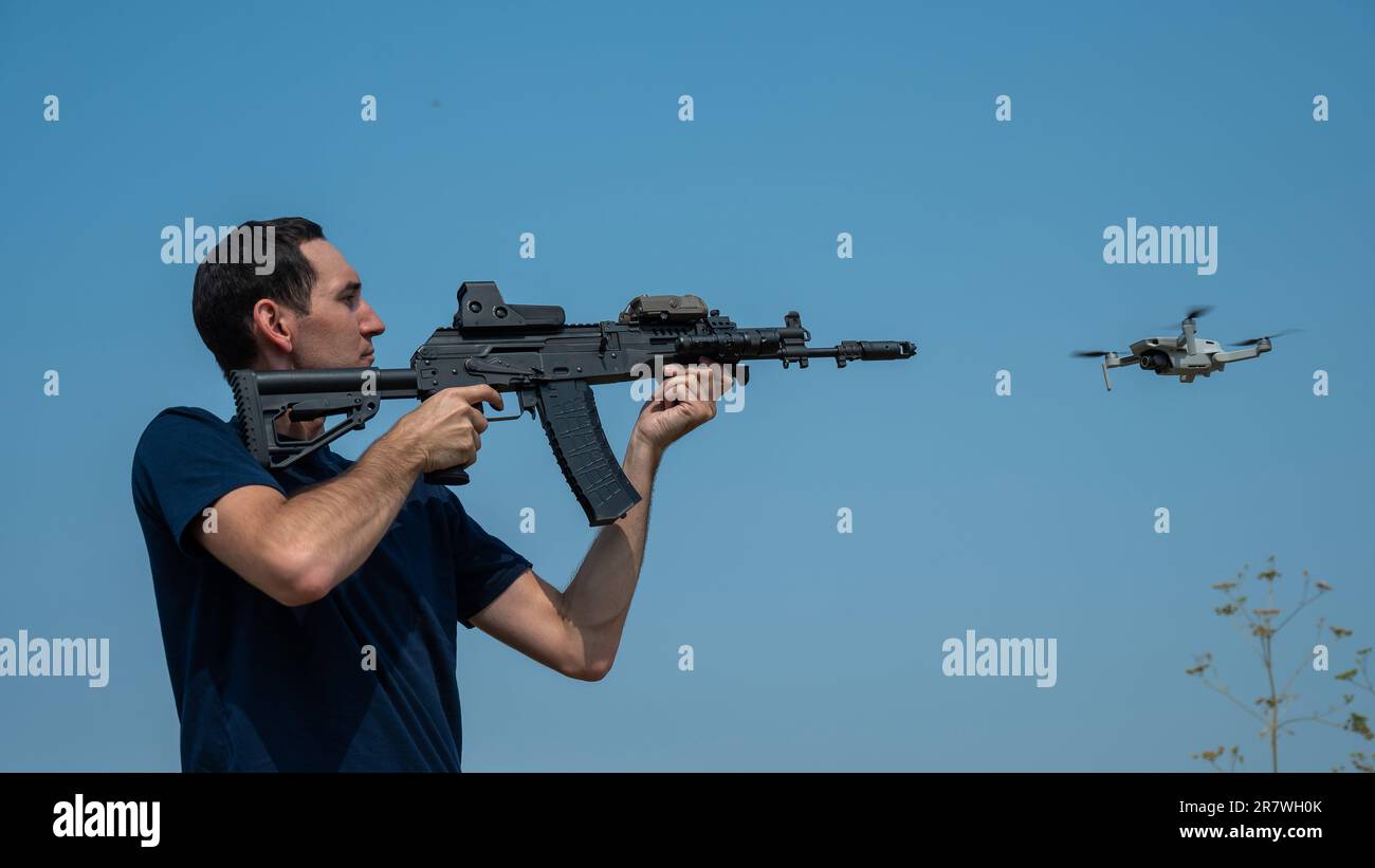 A man aims to shoot a rifle at a flying drone against a blue sky Stock ...