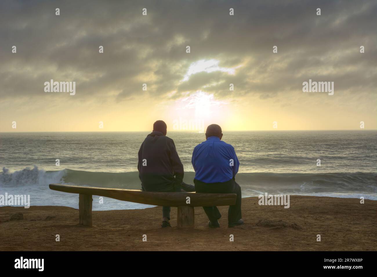 Two elderly men are sitting on a bench by the ocean and watching a ...