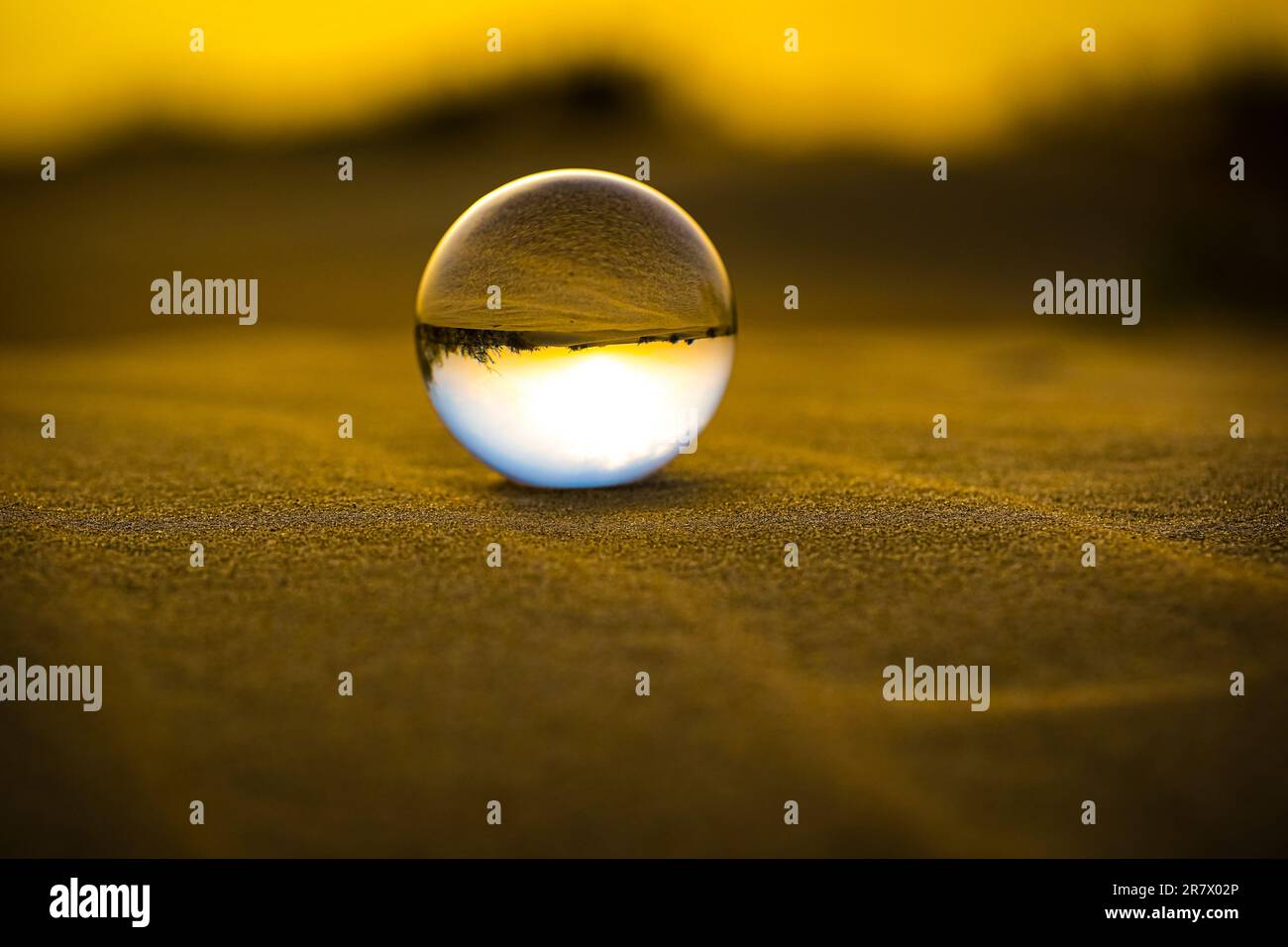 A clear, spherical glass ball rests on the sand, illuminated by light ...