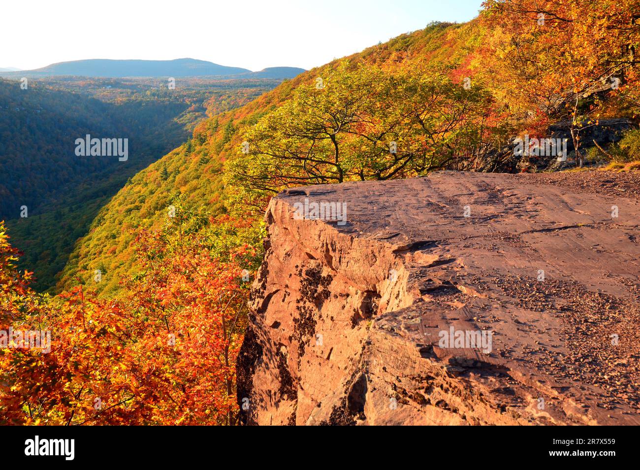 Glowing sunlight strikes a rock outcrop and fall foliage in the ...
