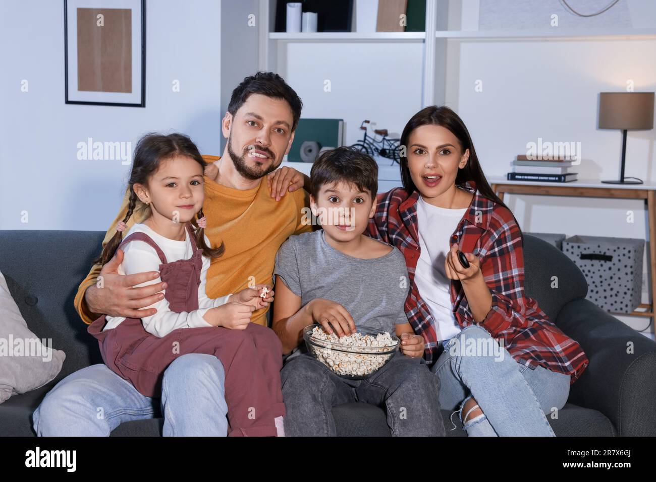 Family watching movie at home in evening. Mother changing TV channels ...