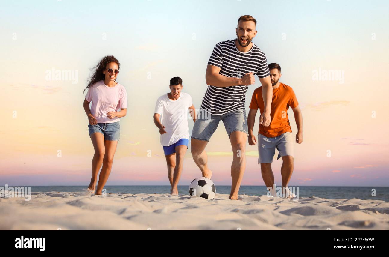 Happy friends playing football on beach during sunset, low angle view ...