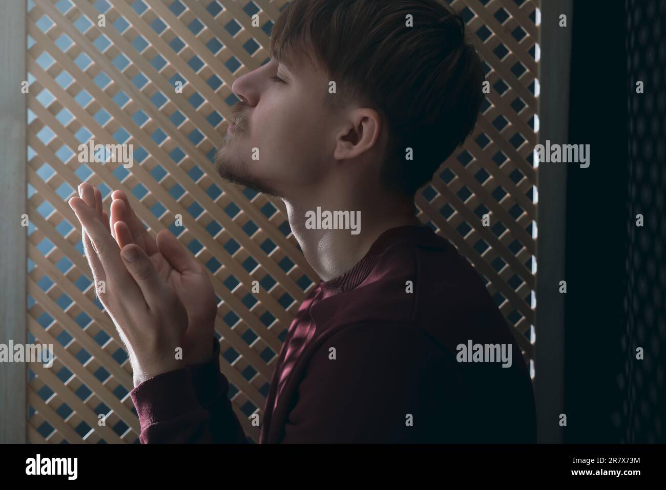 Man praying during confession near wooden window in booth Stock Photo ...