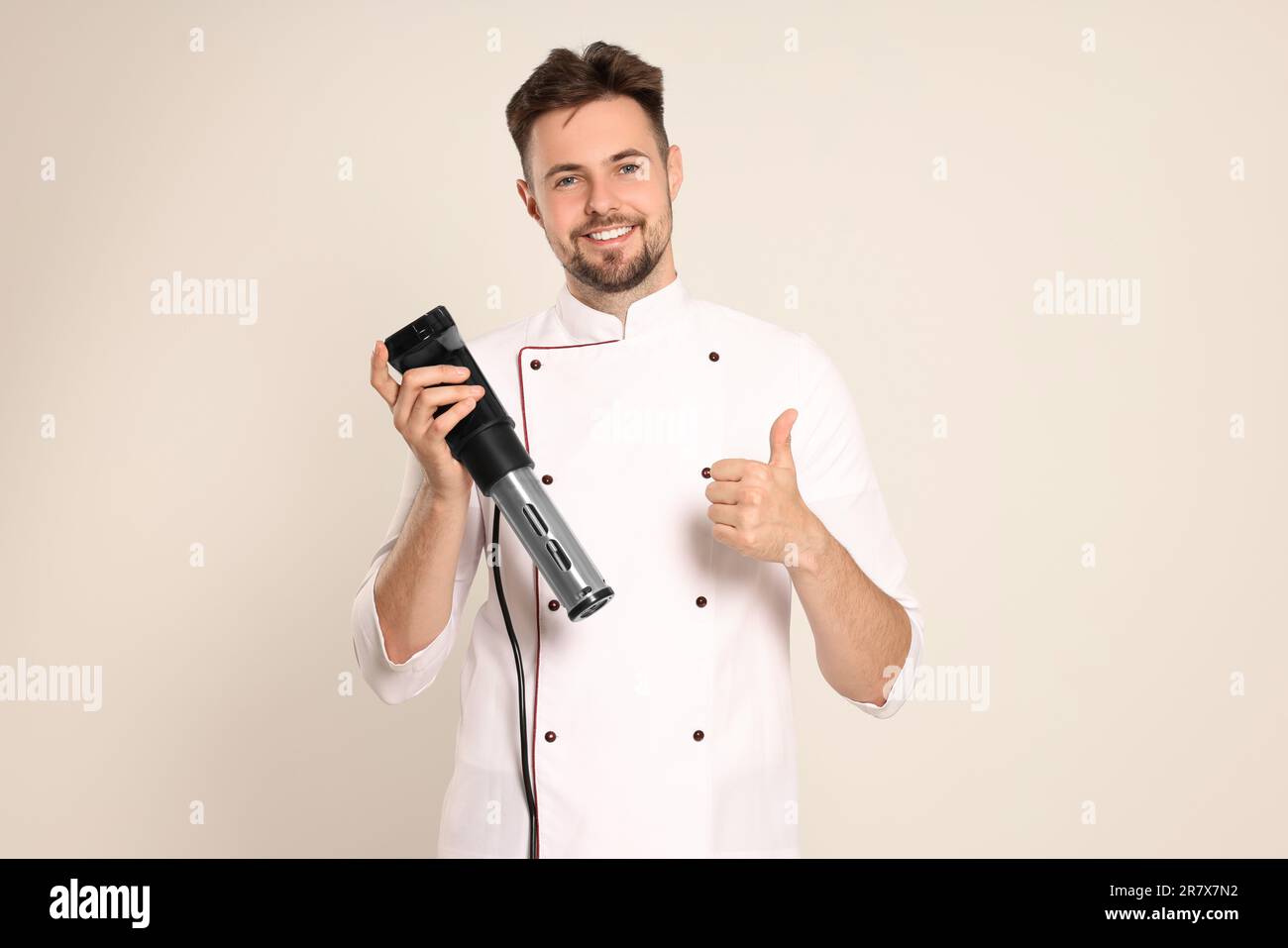 Smiling chef holding sous vide cooker and showing thumb up on beige ...