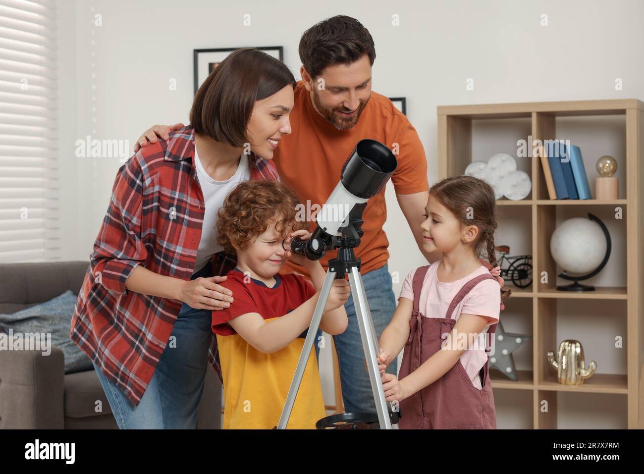 Happy family looking at stars through telescope in room Stock Photo - Alamy